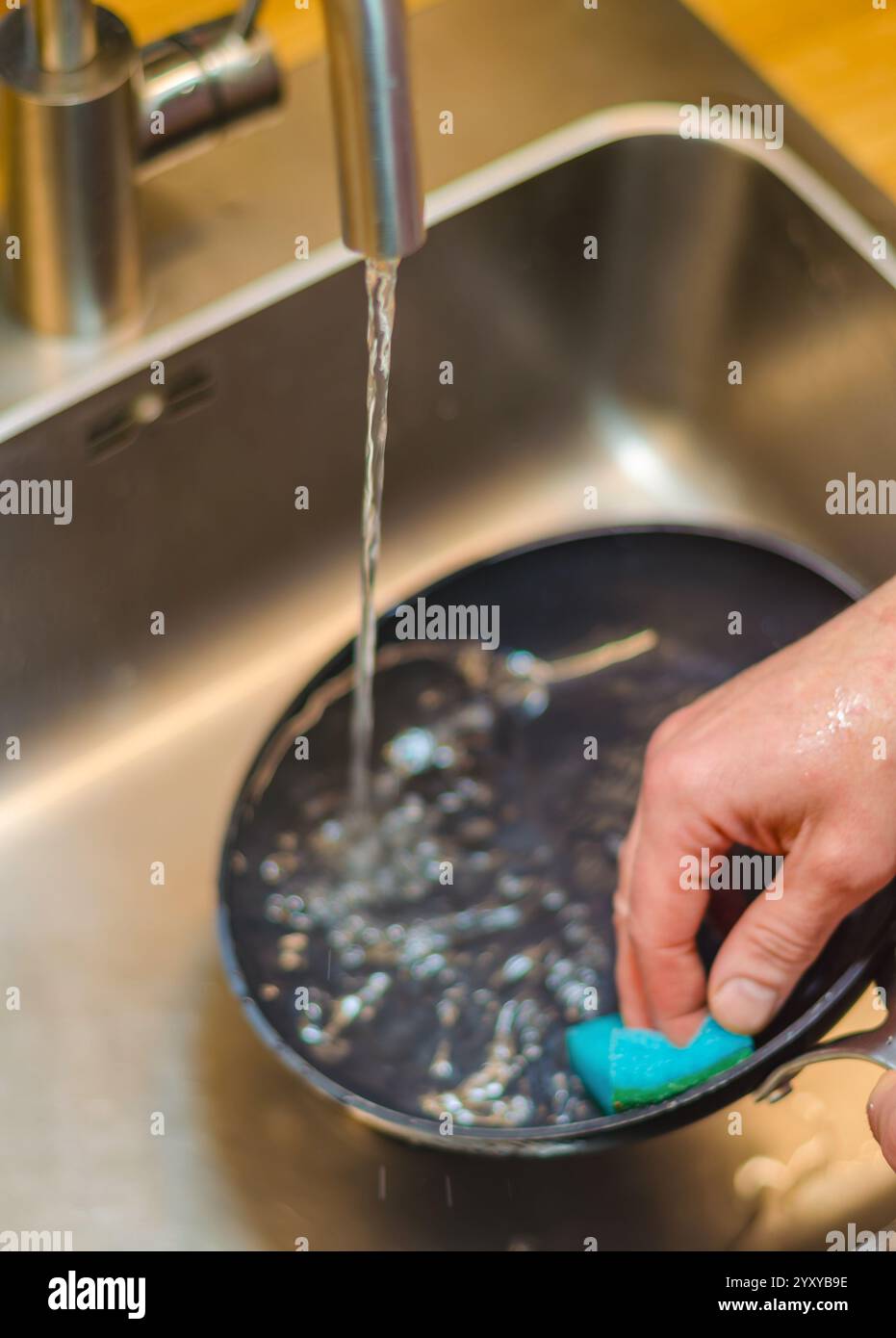 hand washing a black frying pan in a stainless steel sink with a blue ...