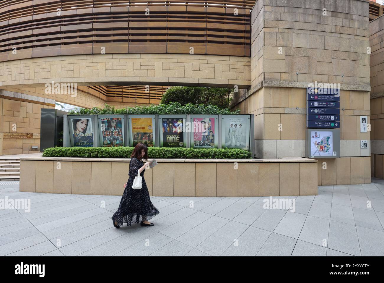 Woman using mobile phone walking past movie posters in the Roppongi ...
