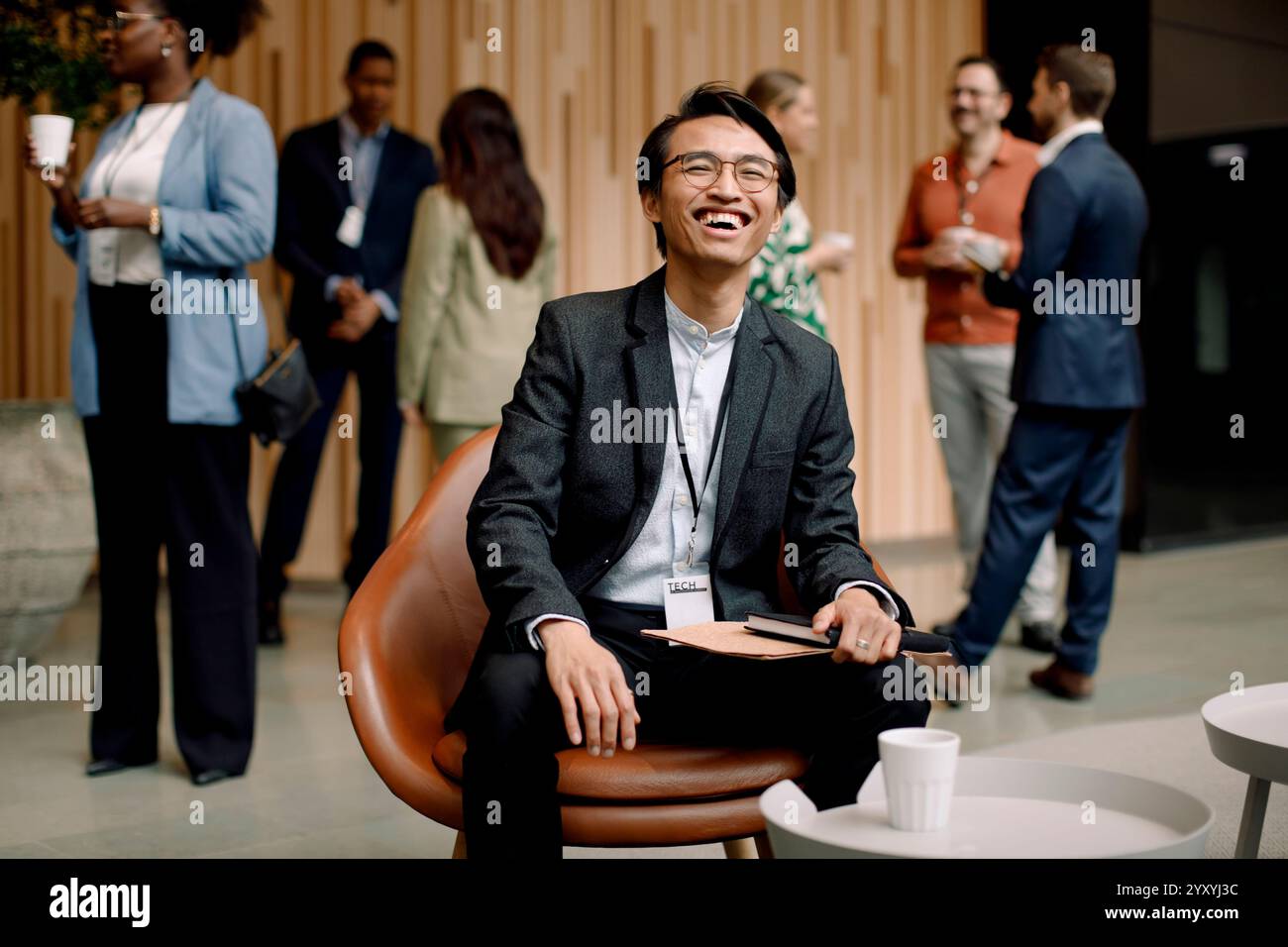 Happy male entrepreneur laughing while sitting on chair at convention ...