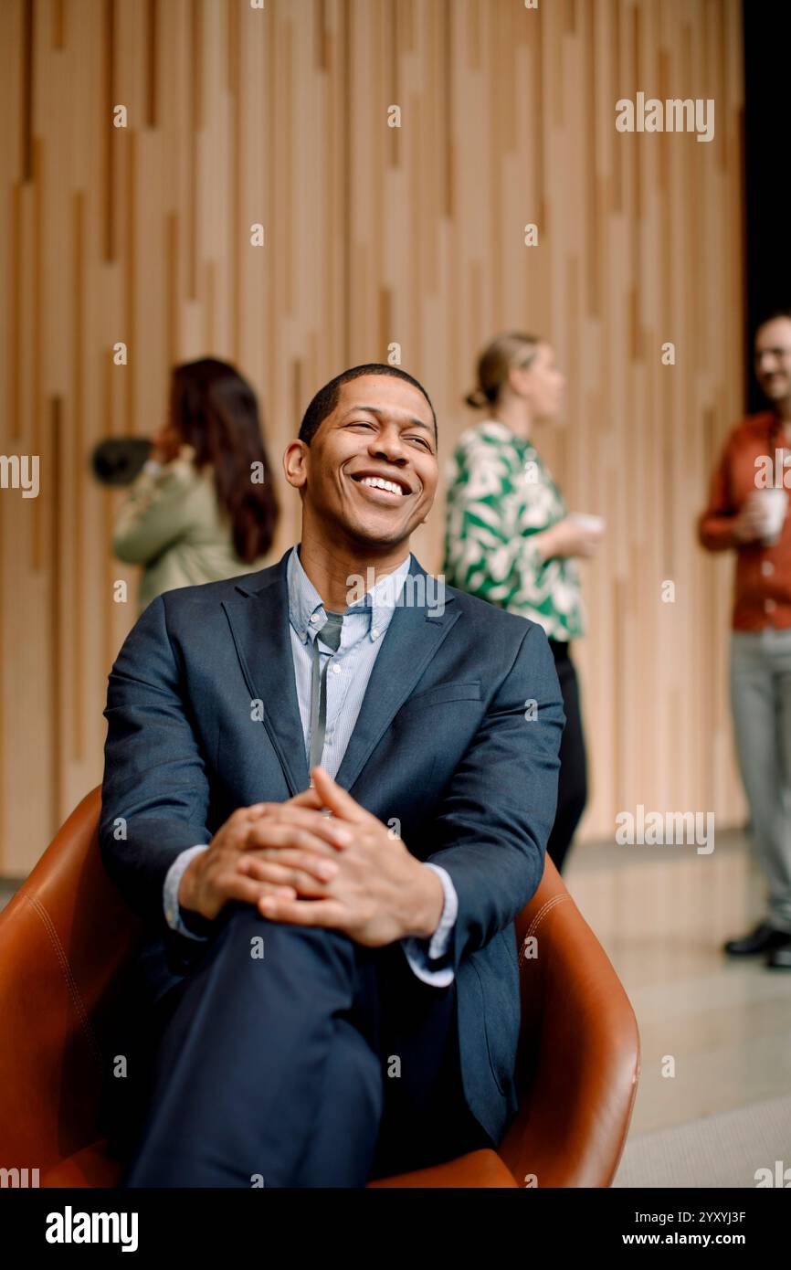 Smiling male entrepreneur sitting with eyes closed on chair at ...