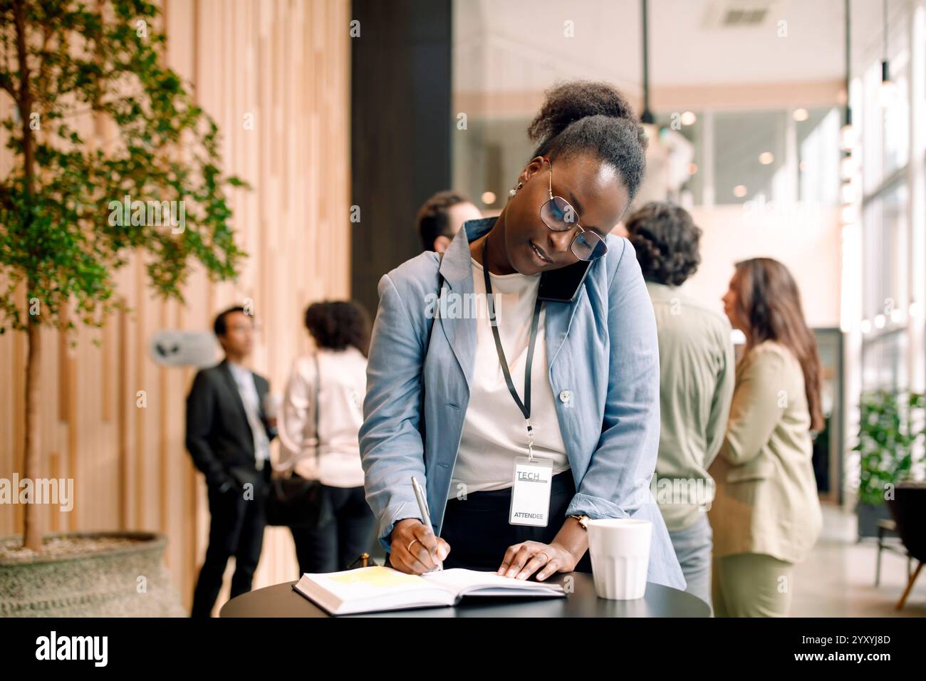 Female entrepreneur talking through smart phone while writing in diary ...