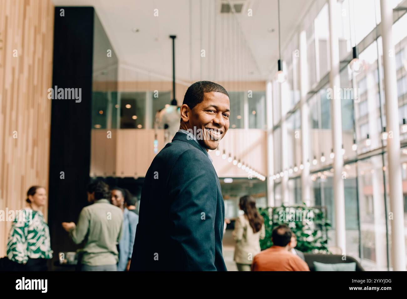 Portrait of smiling mature businessman looking over shoulder in lobby ...