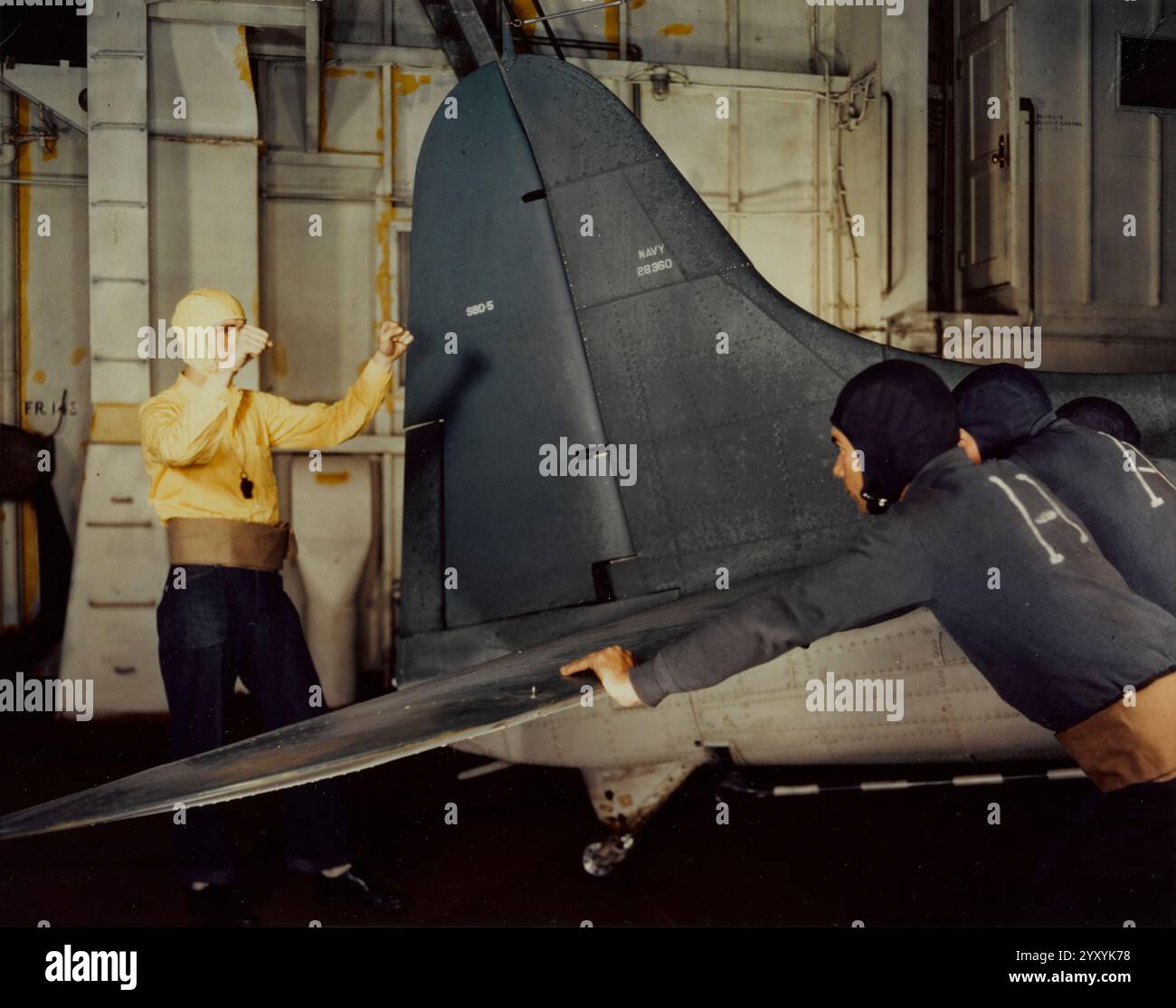 A U.S. Navy plane director (in yellow cap and jersey) guides plane ...