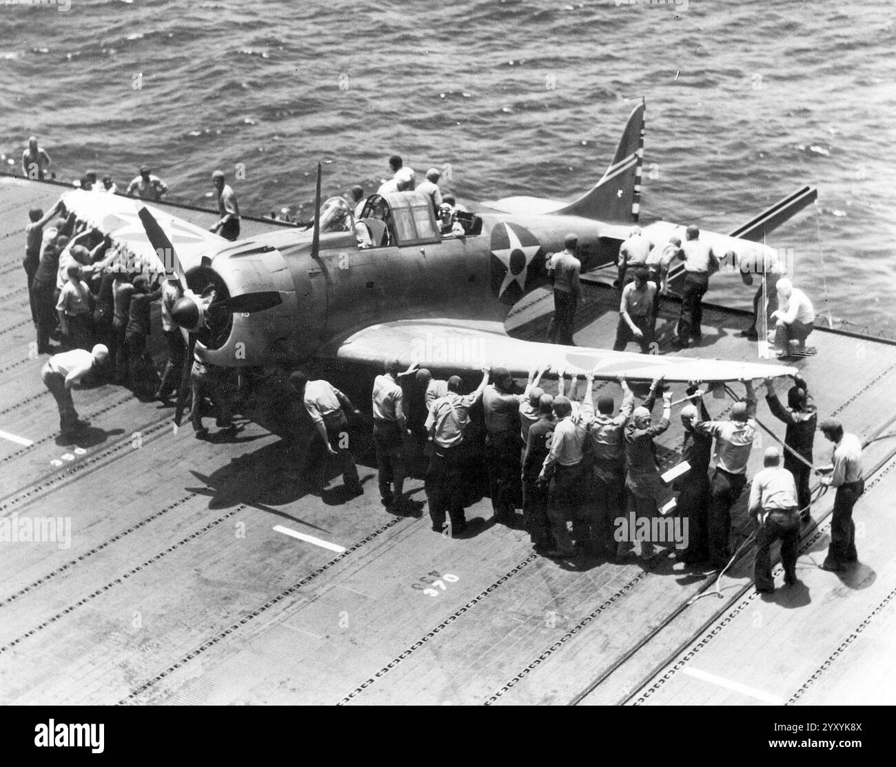 U.S. Navy flight deck personnel maneuver a Douglas SBD-3 Dauntless of ...