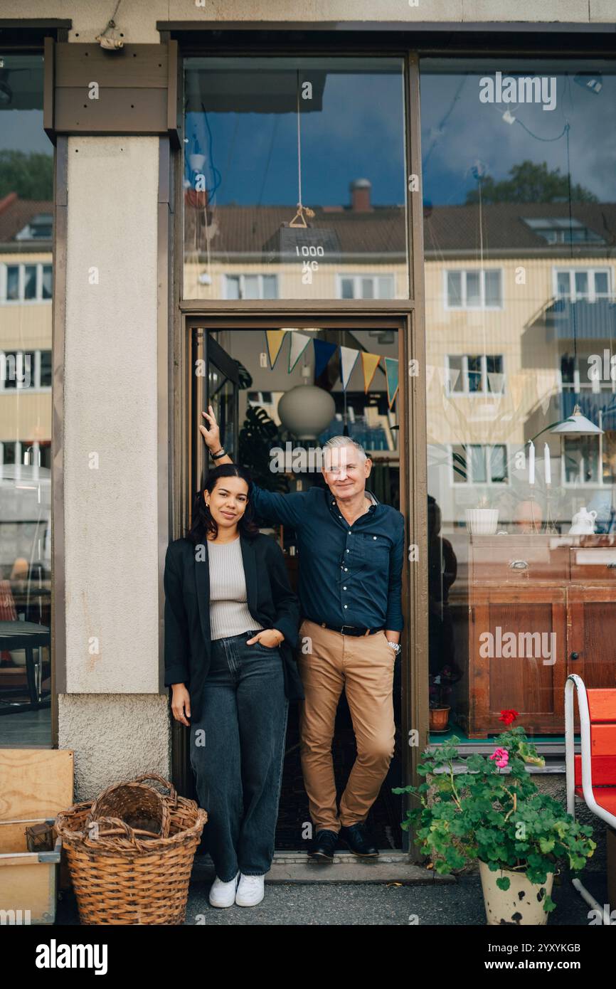 Portrait of smiling male and female owners standing at doorway of ...