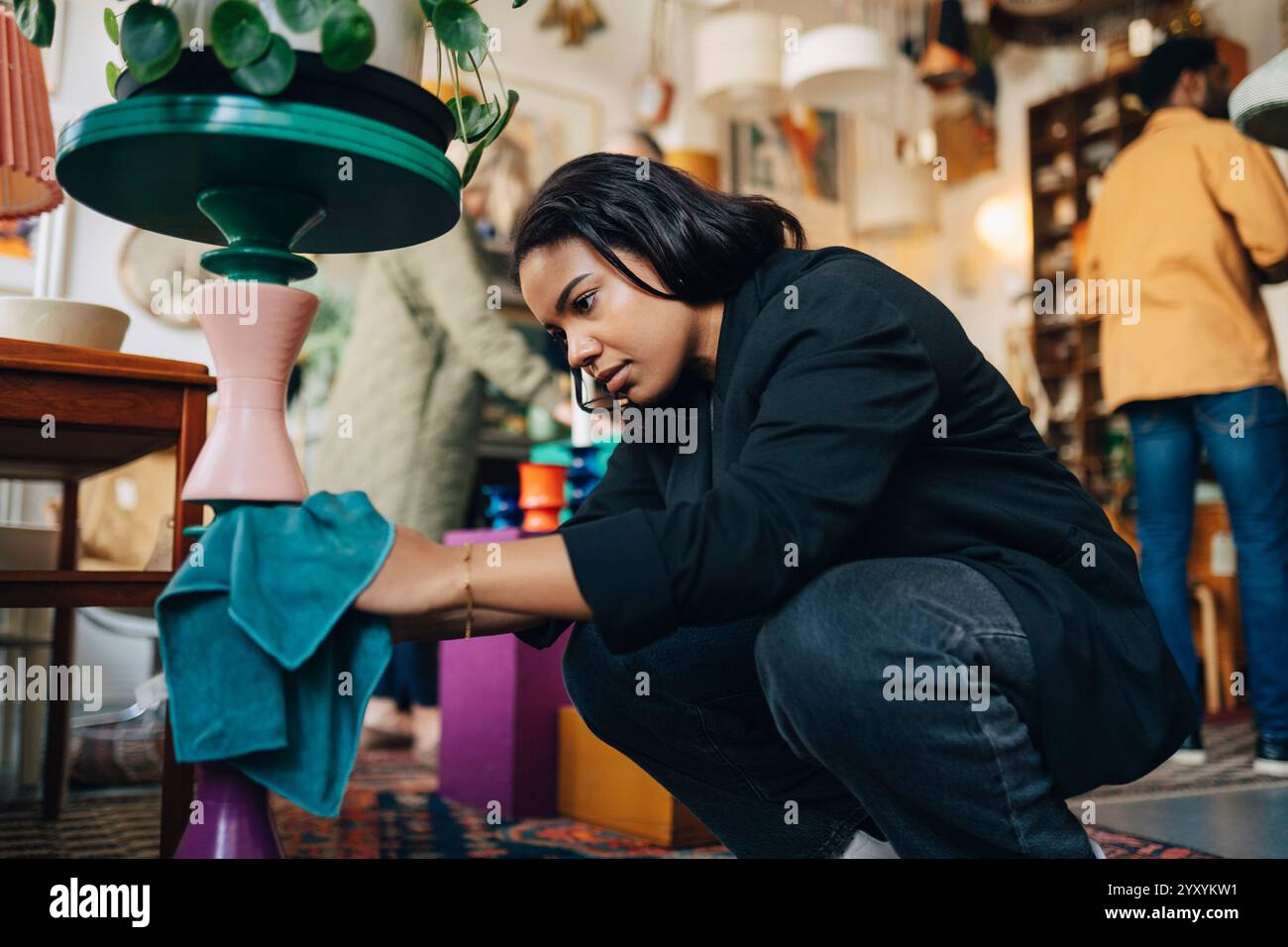 Female entrepreneur cleaning merchandise with rag while crouching at ...