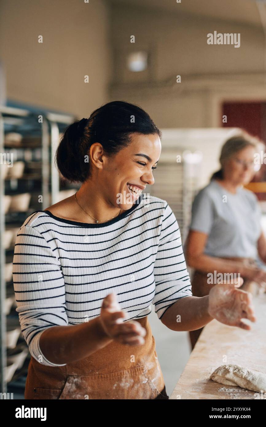 Happy female baker laughing while kneading dough at bakery Stock Photo ...
