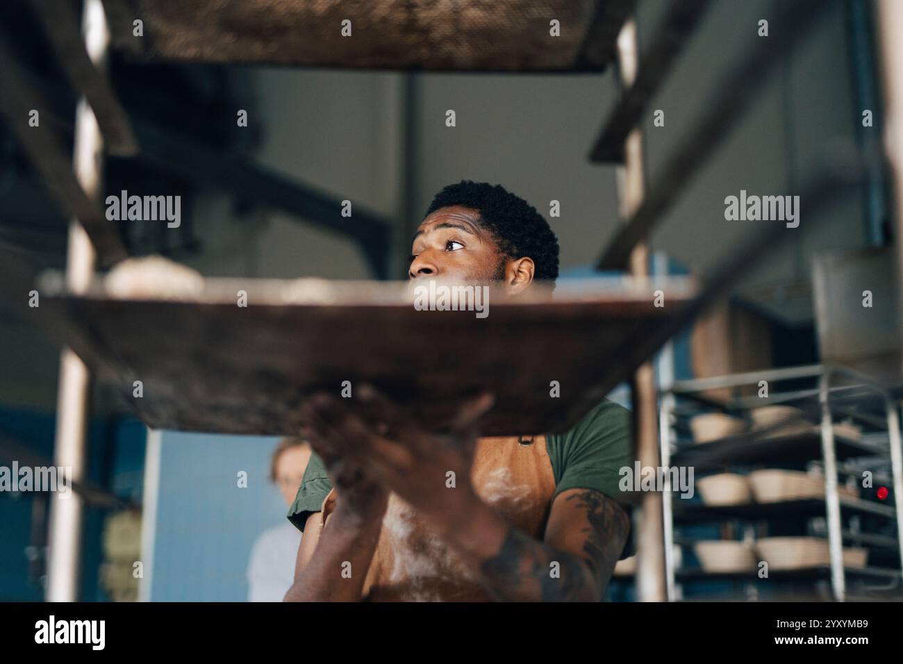 Male baker removing tray from cooling rack while working at bakery ...