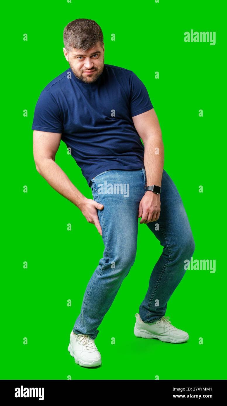 A man in a blue shirt and jeans awkwardly poses against a bright green ...