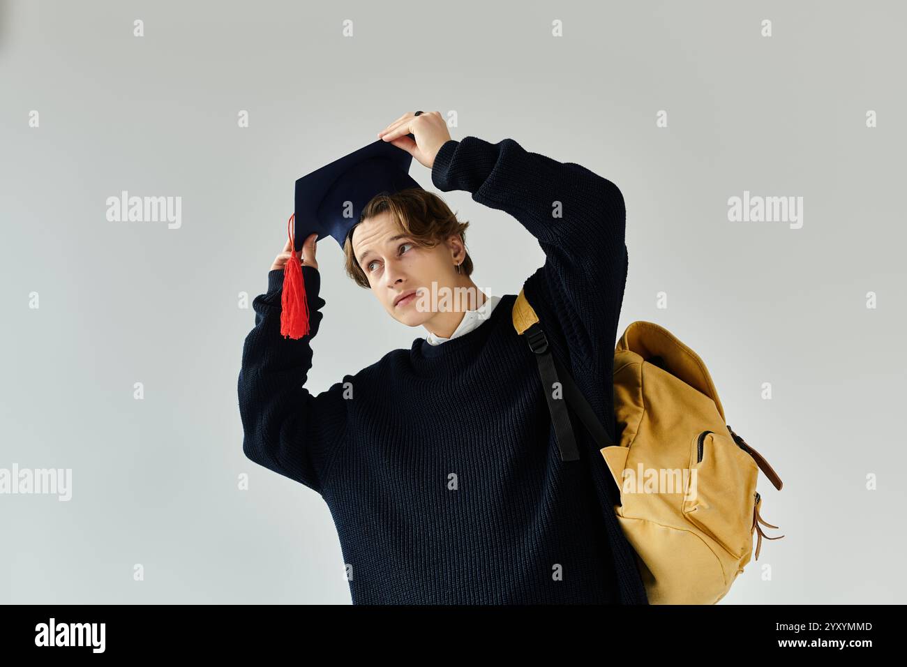 A young man adjusts his graduation cap while showcasing his college ...