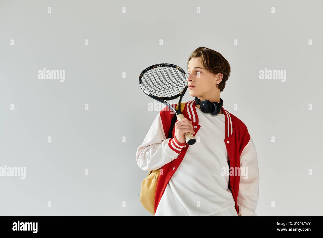 A stylish young man holds a tennis racket in a studio, exuding ...