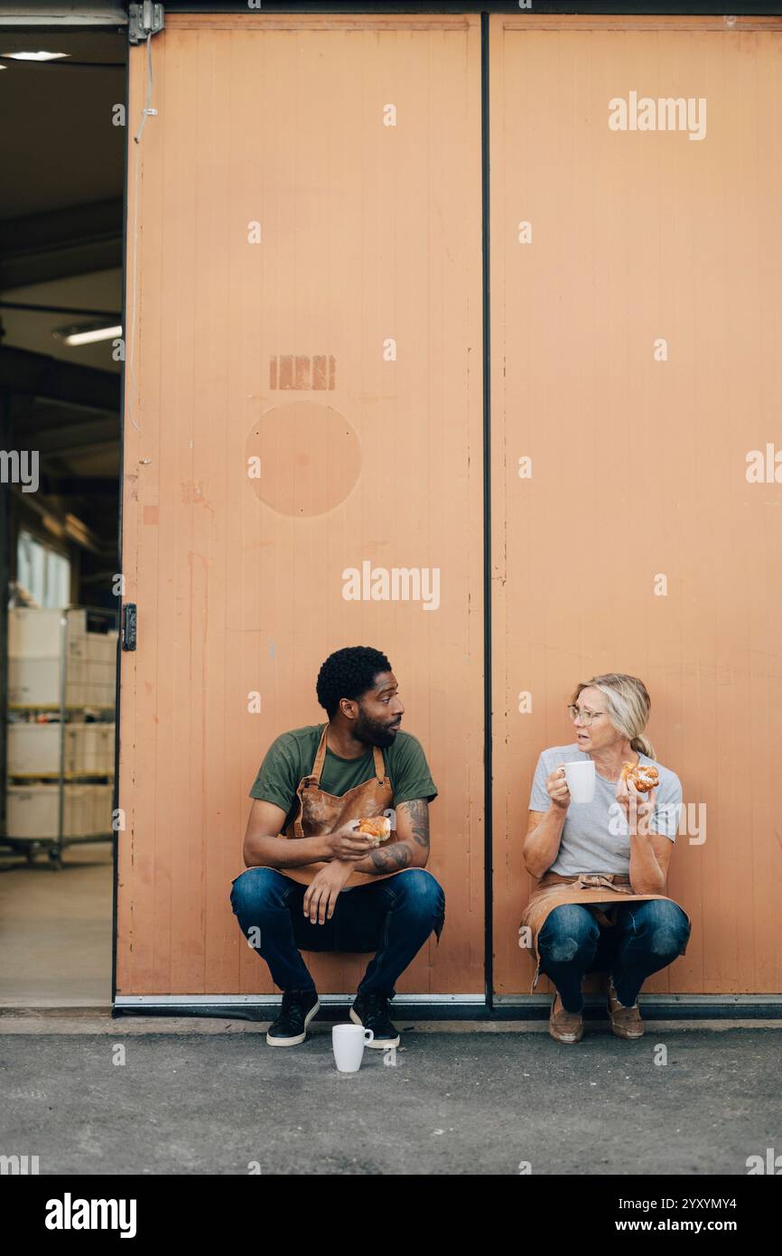 Male and female bakers talking with each other while having snacks ...