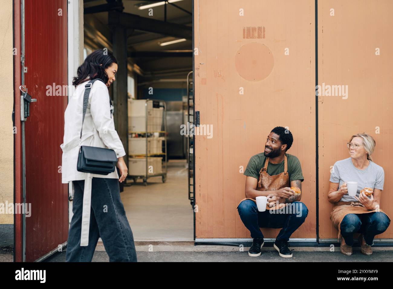 Male and female bakers greeting customer arriving during coffee break ...