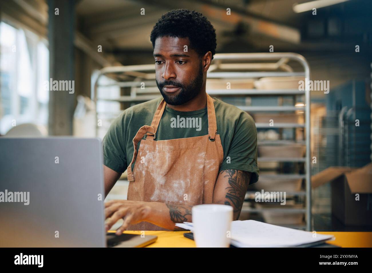 Male baker wearing apron and working on laptop at bakery Stock Photo ...