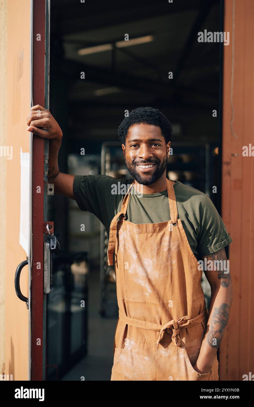 Portrait of confident male baker standing with hand in pocket at bakery ...