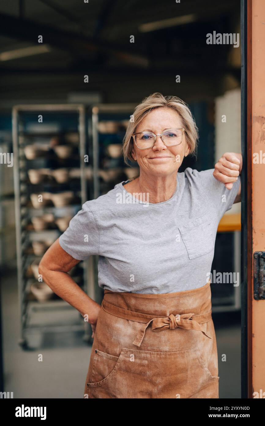 Confident senior female baker standing with hand on hip at bakery ...