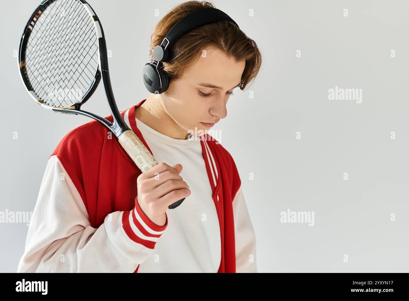 A handsome student wearing a bomber jacket holds a tennis racket, lost ...