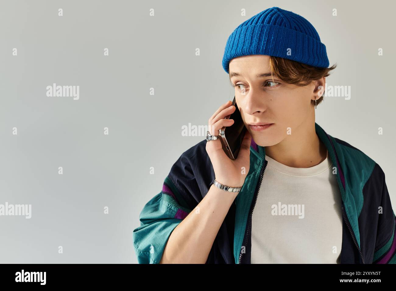 A young man wearing a bomber jacket is engaged in a phone conversation ...