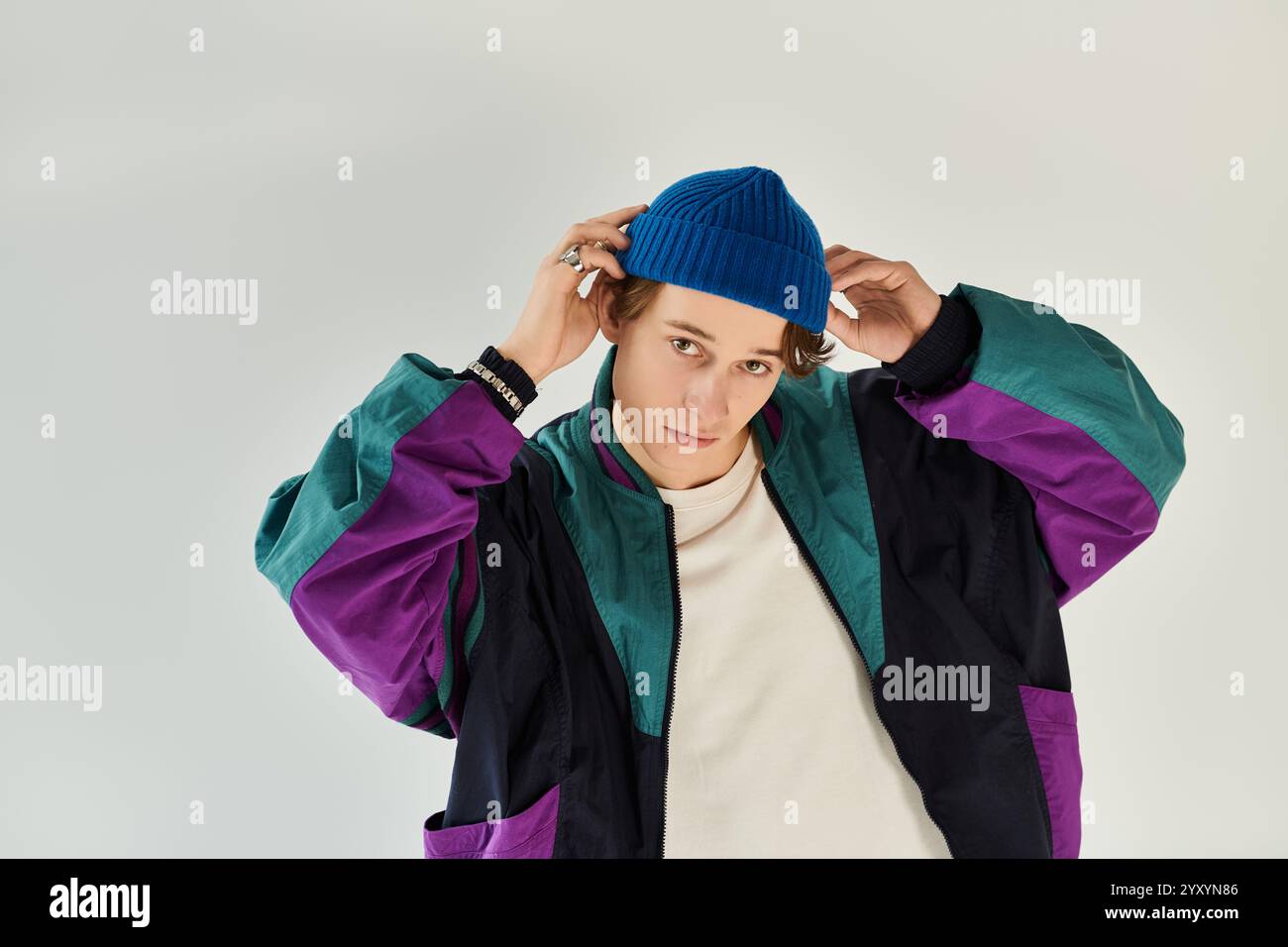 A handsome young man adjusts his blue beanie while wearing a vibrant ...