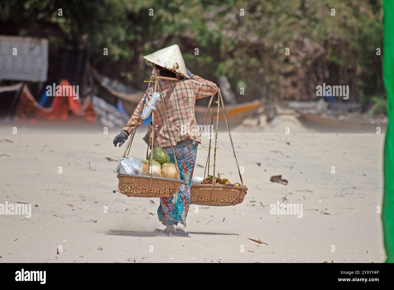 Vietnamese street vendor walking on sandy beach with traditional ...