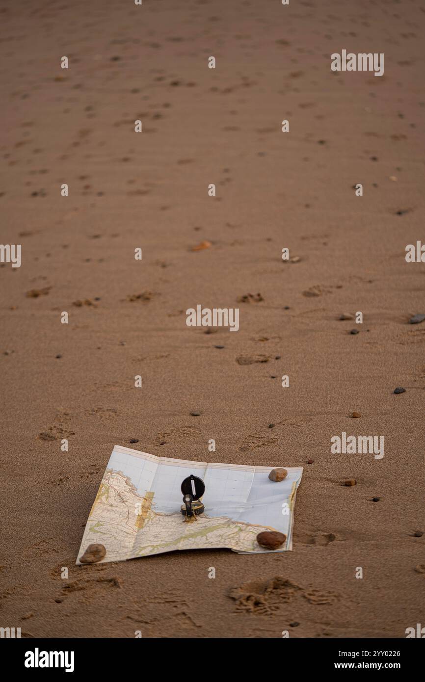 map and prismatic compass weighted down with pebbles on a sandy beach ...