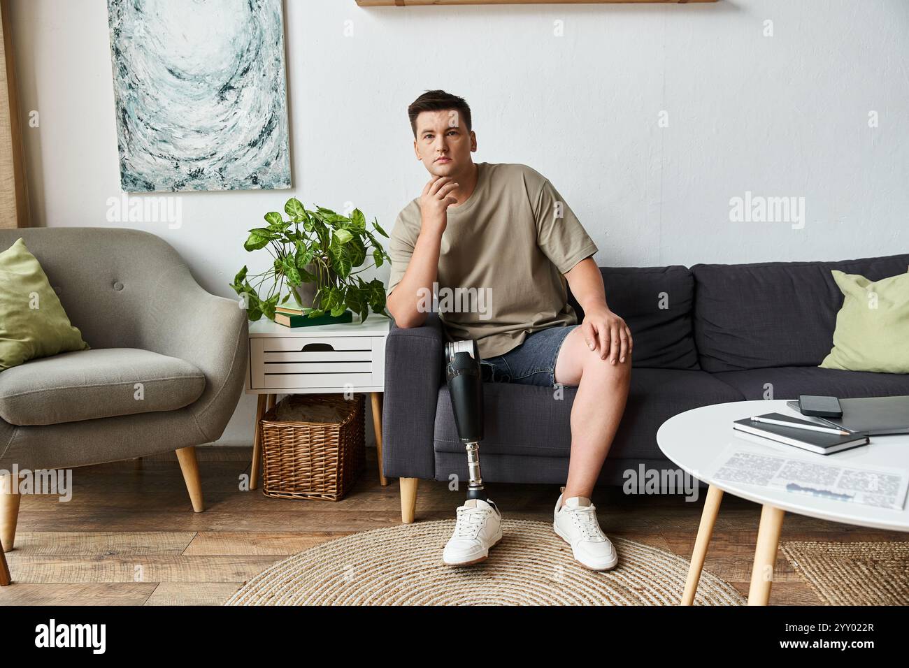 Handsome young man relaxes on a couch, hand on chin, in stylish living ...