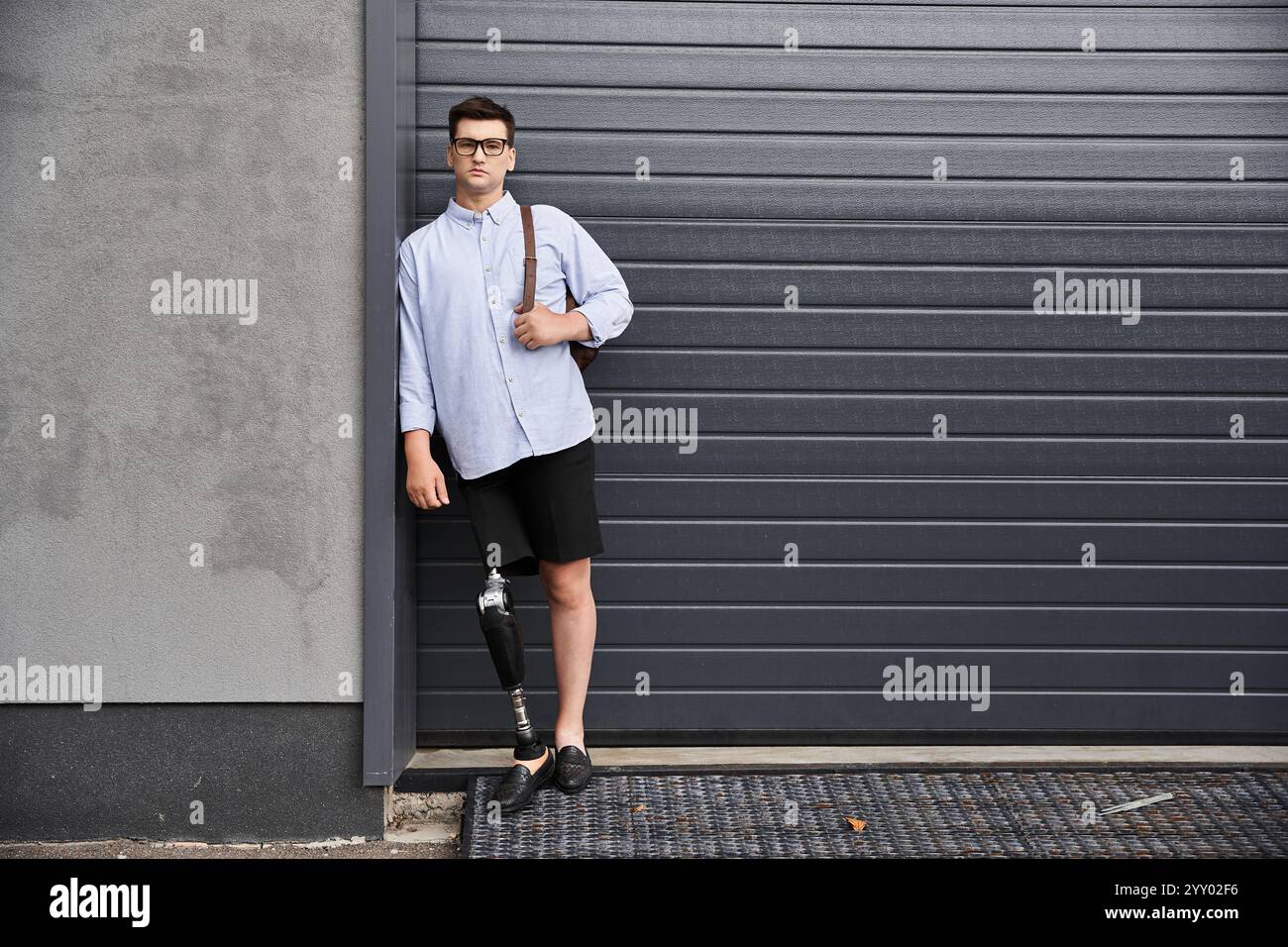 A young man with a prosthetic leg leans casually against a garage wall ...