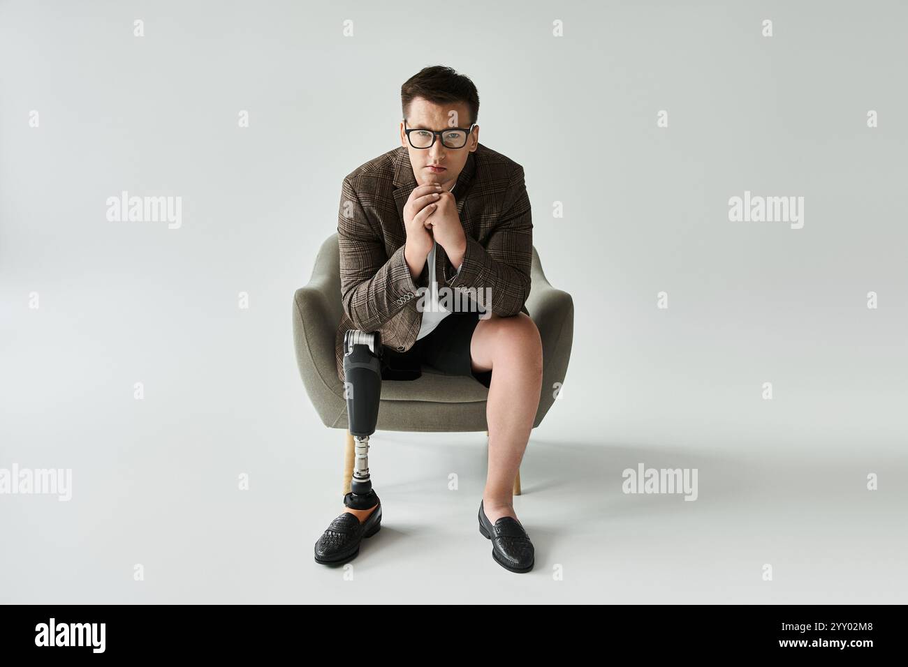 Young man with a prosthetic leg sits thoughtfully in a stylish chair ...