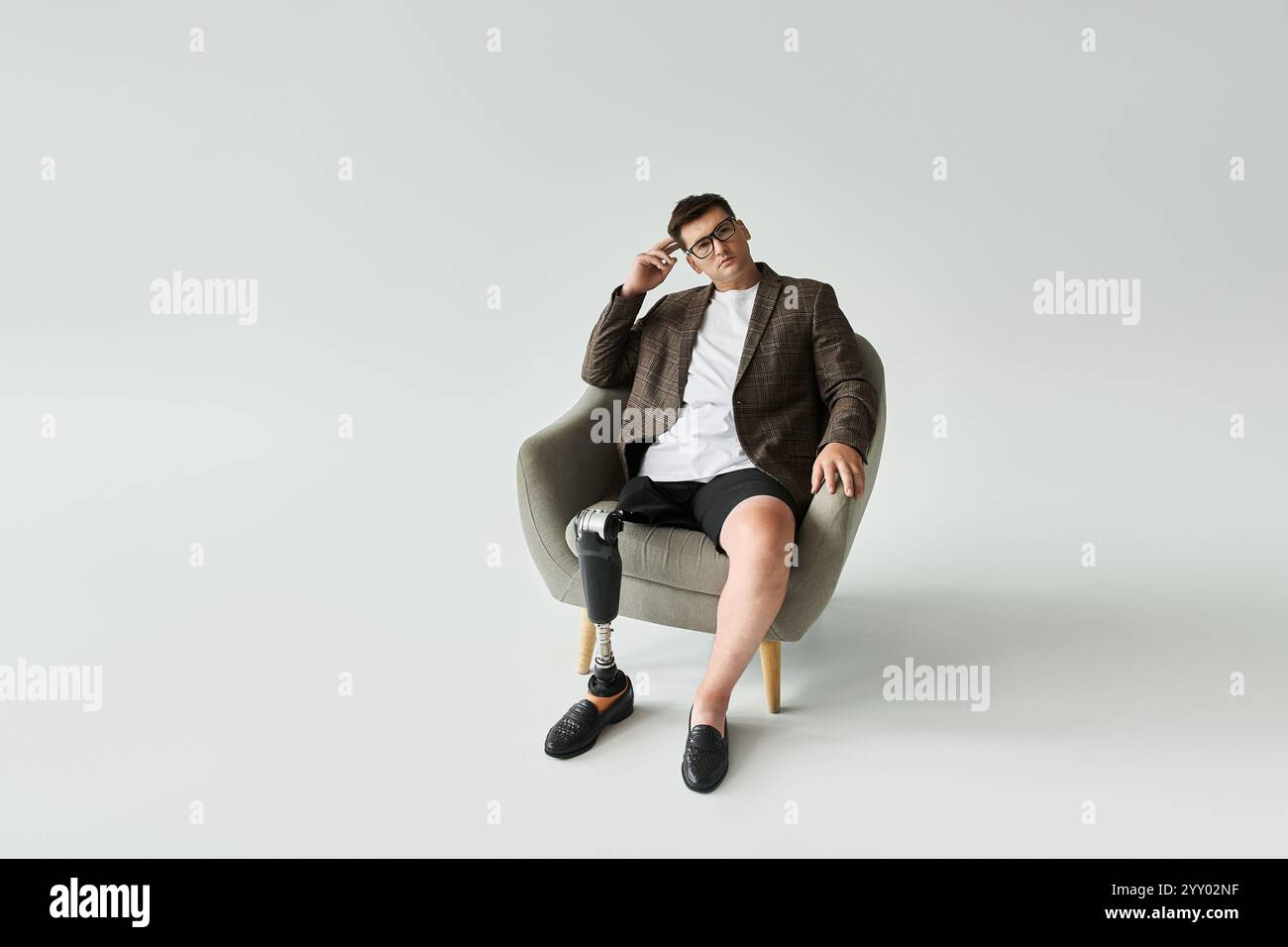 A young man with a prosthetic leg is seated in a modern chair, deep in ...