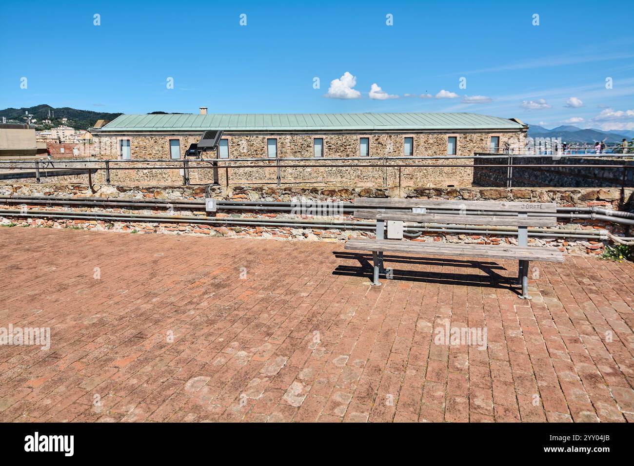 Outdoor bench on a brick-paved rooftop with industrial pipes and a ...