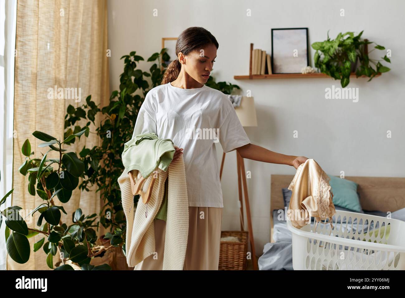 A young African American woman tidies her room, sorting laundry and ...