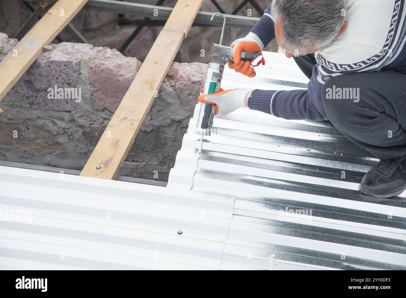 Worker using glue gun with adhesive to fix the metal steel on the roof ...