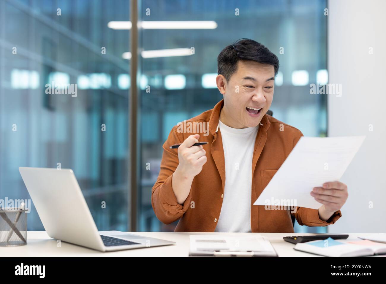 Asian man expressing excitement over positive outcomes while working at ...