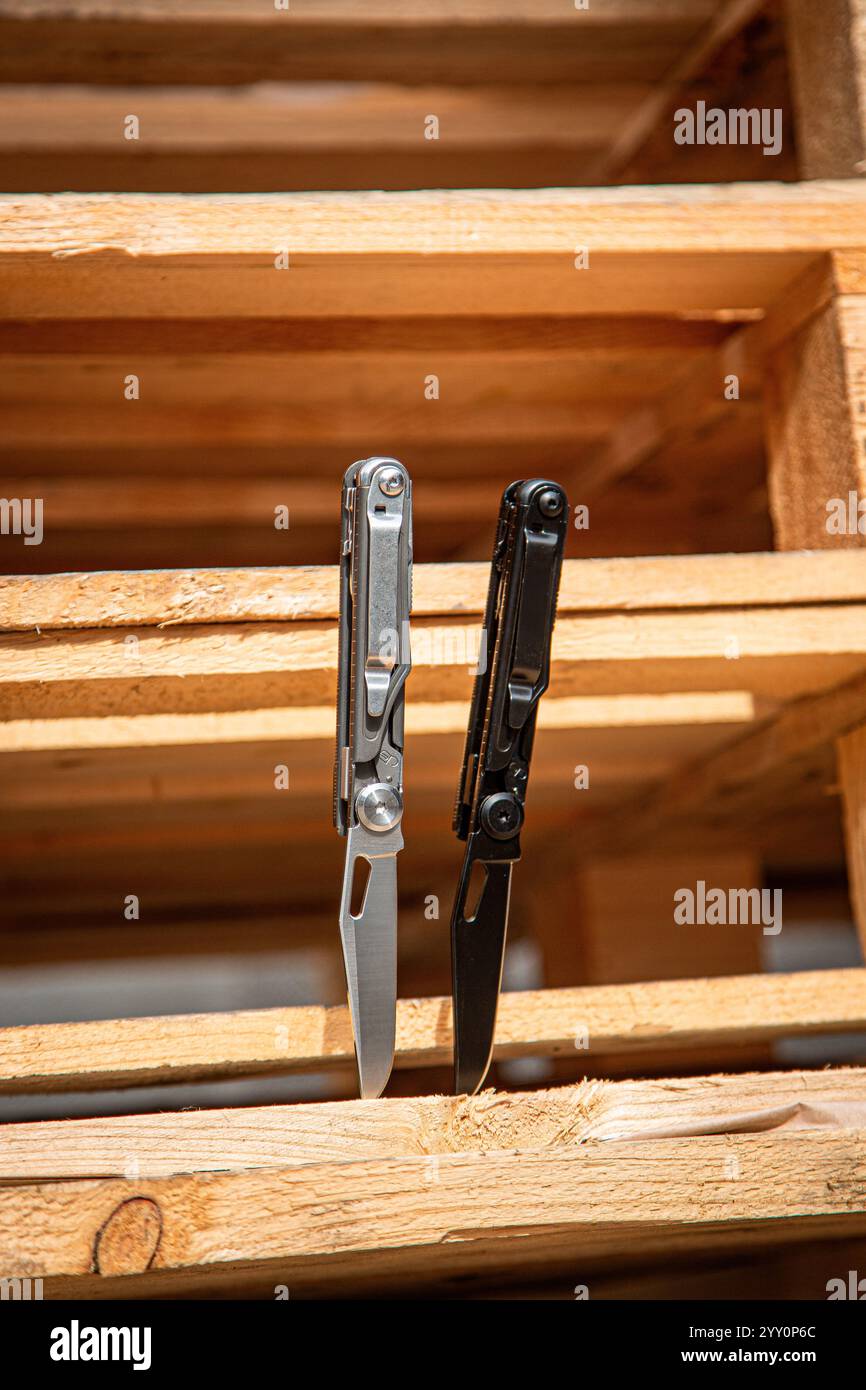 Two multitools with open blades, one silver and one black, are stuck ...