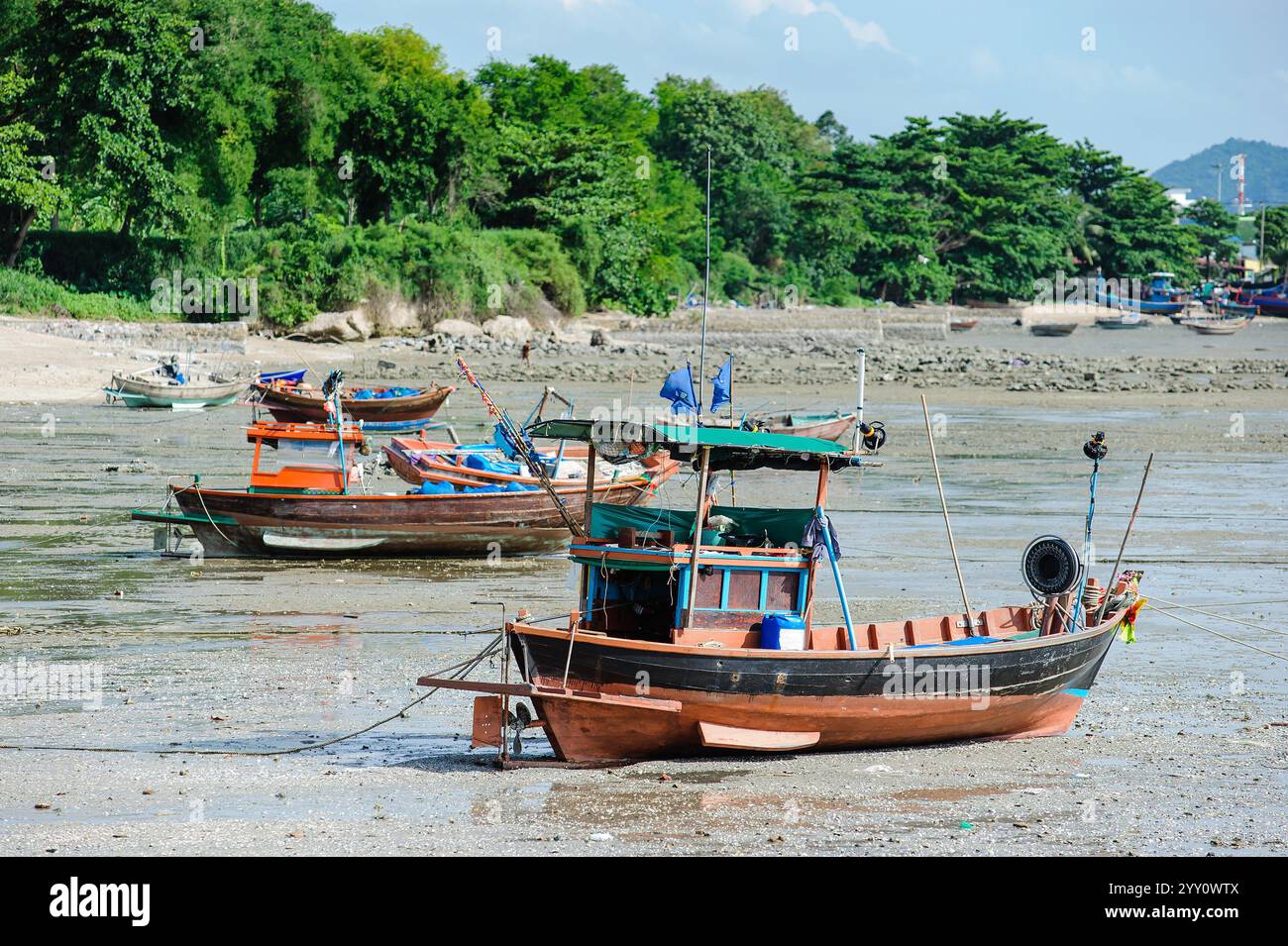 many empty Thai fishing boats lay down on a sea base next to the beach ...