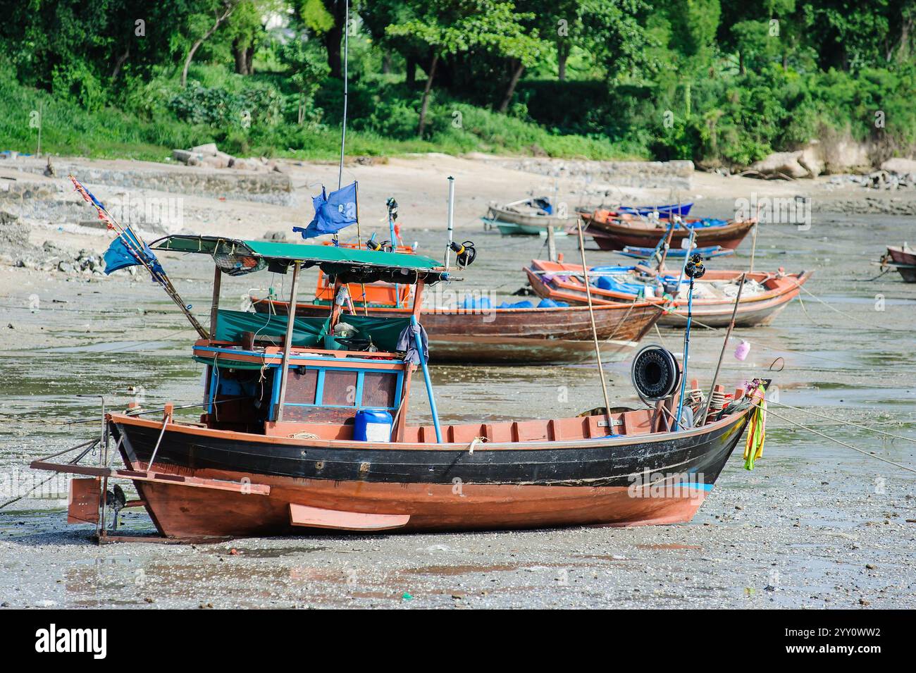 many empty Thai fishing boats lay down on a sea base next to the beach that run out of seawater ...