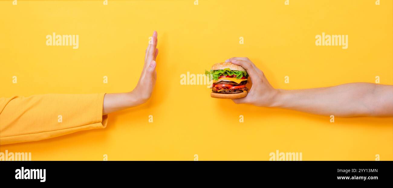 Hand gesturing rejection of fast food hamburger on yellow color banner ...