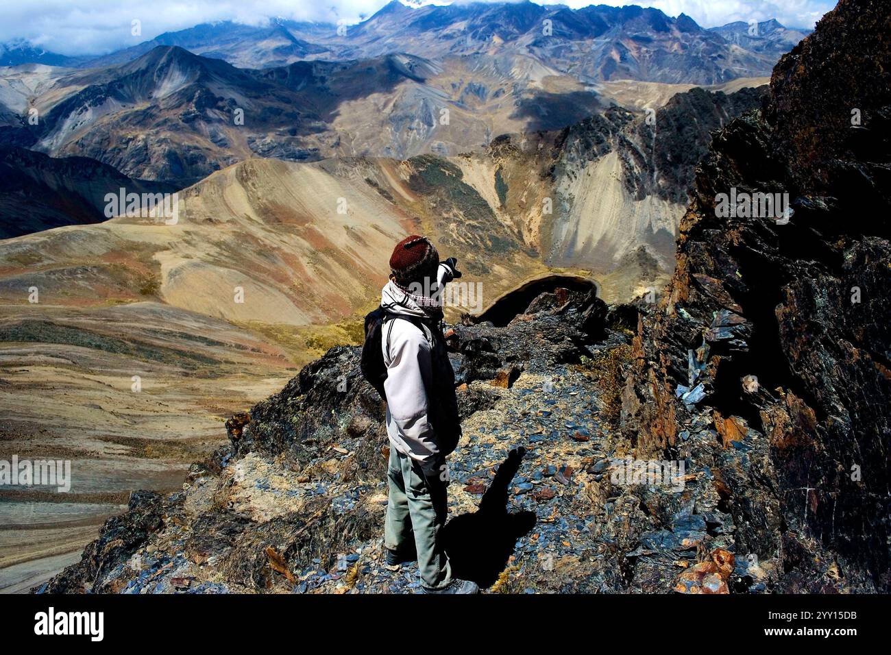 Hiker in the Bolivian Andes stands on a rocky outcrop in the Bolivian ...