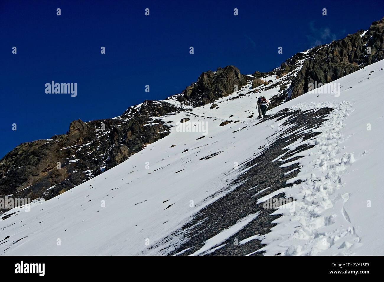 Two hikers ascend a snow-covered slope in Bolivia, surrounded by rugged ...