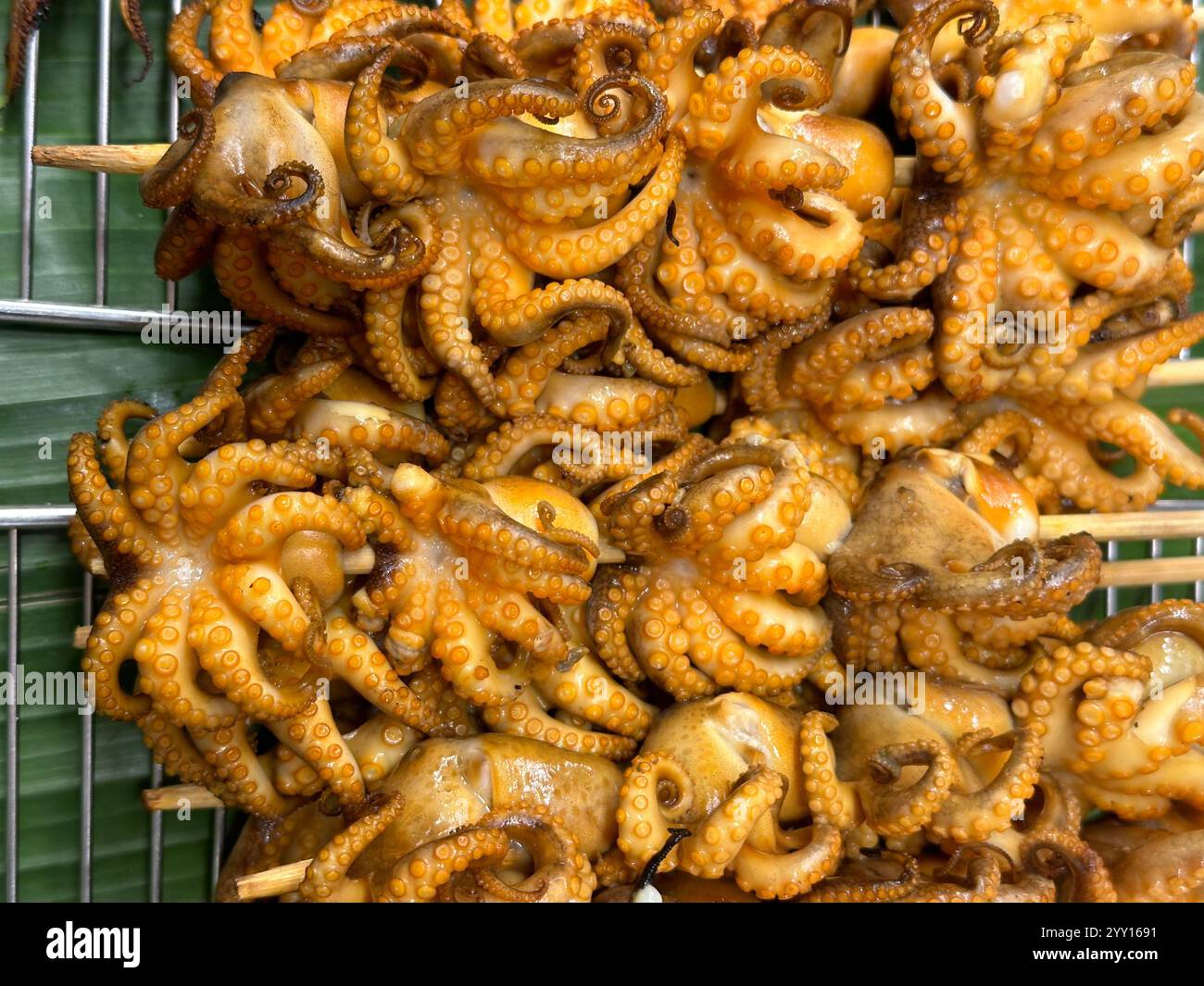 A heaping pile of deliciously fried octopus skewers cooking on a grill ...