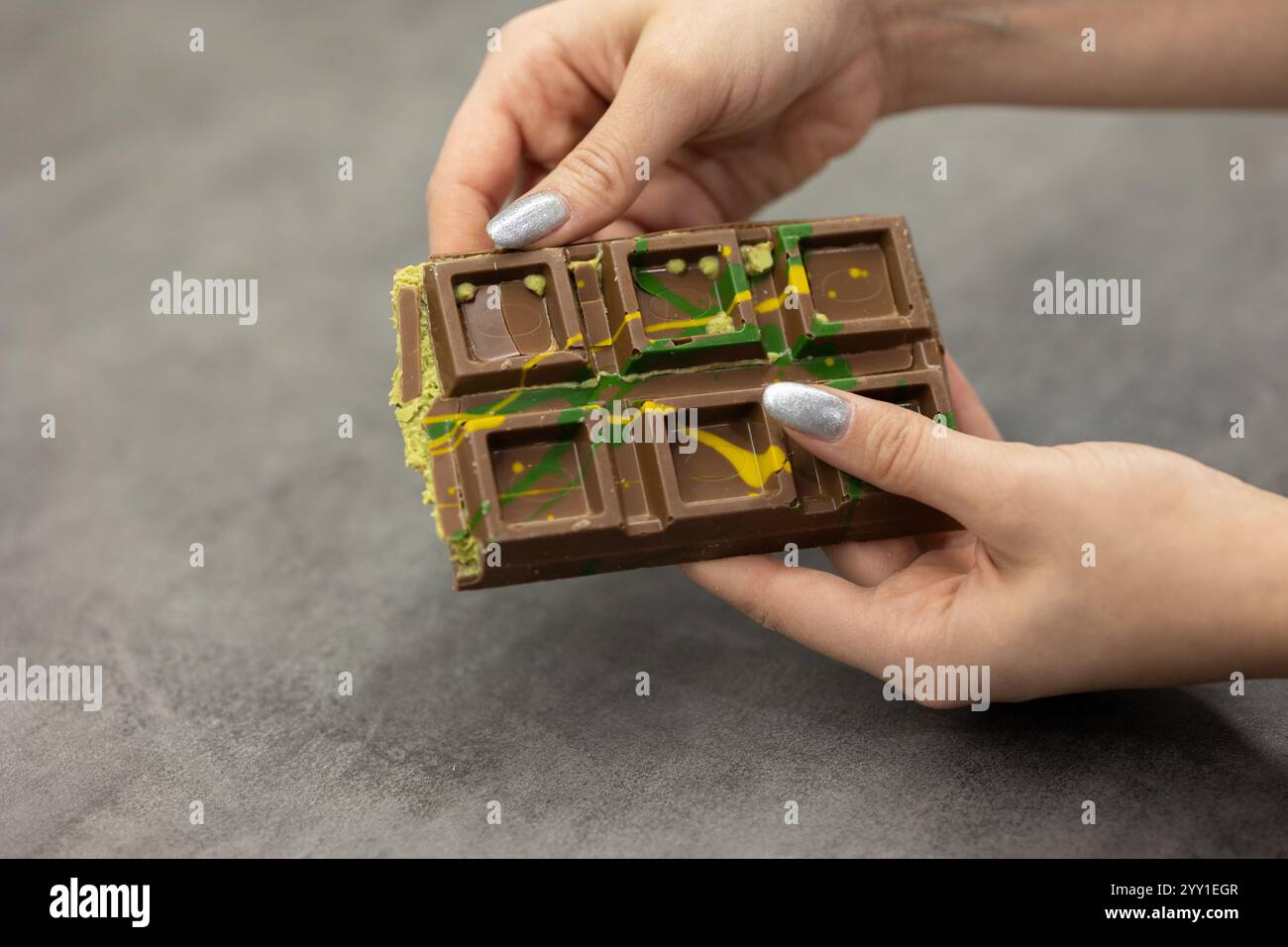Female hands breaking off piece of Dubai chocolate on gray background ...