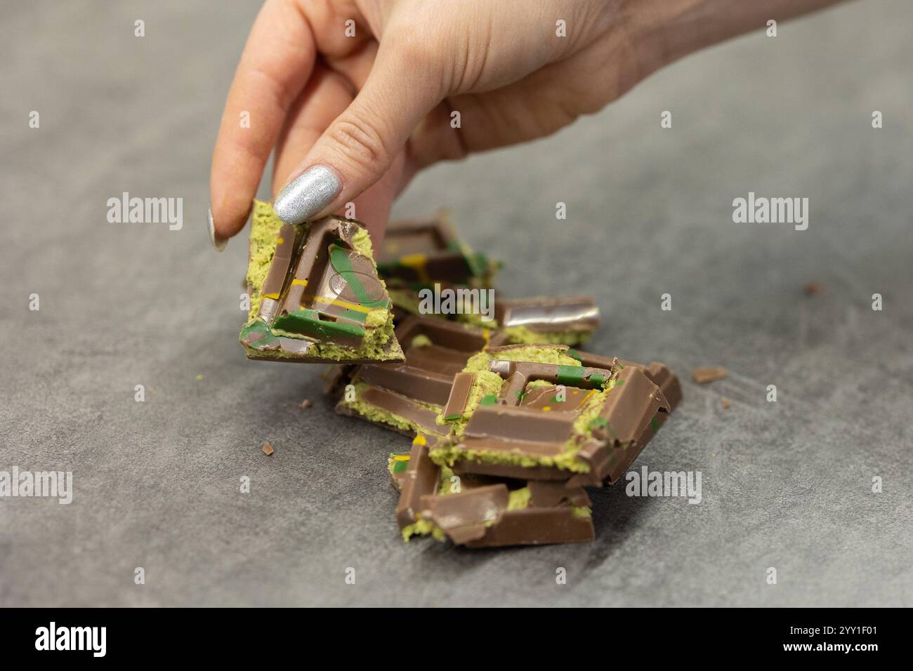 Female hands breaking off piece of Dubai chocolate on gray background ...