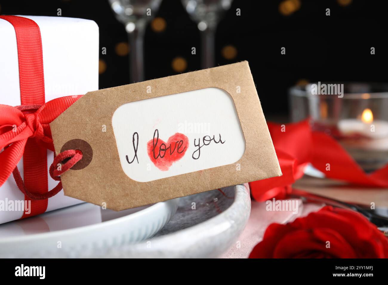 Beautiful place setting and tag with phrase I Love You on table against blurred lights, closeup ...