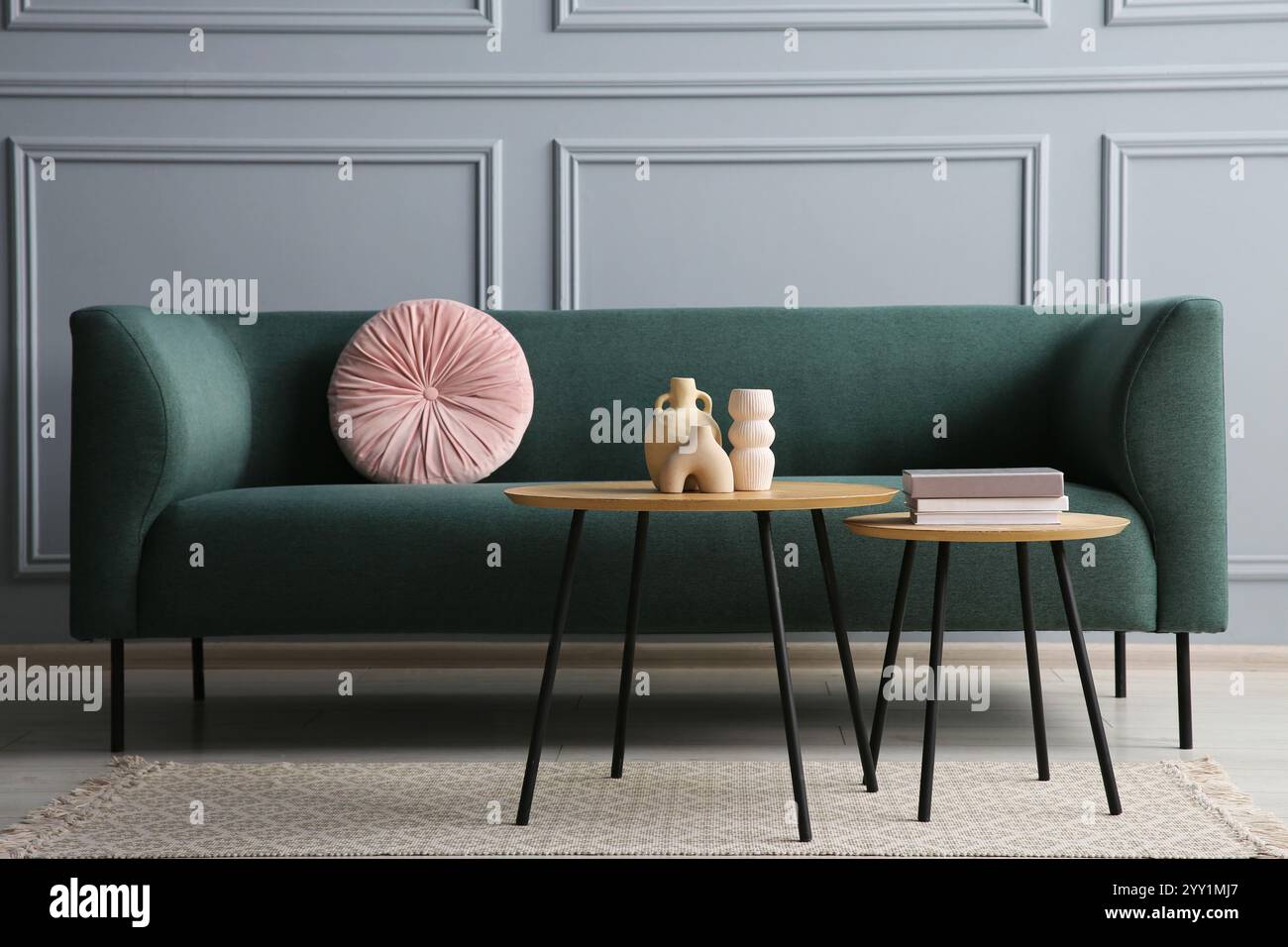 Stylish sofa with cushion, books and decor elements on nesting tables ...