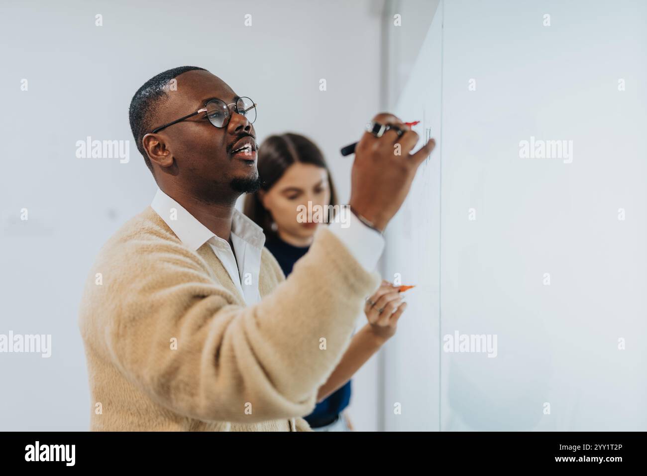 Two colleagues collaborate on a whiteboard, sharing ideas and ...