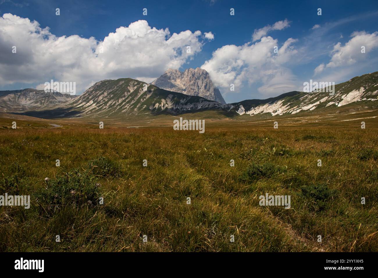 Expansive mountain valley with a dramatic rocky peak under a bright ...