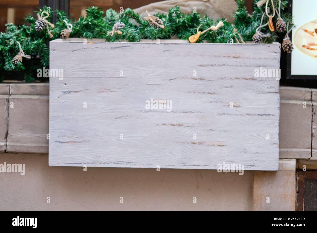A blank wooden sign is positioned in front of lush greenery and festive ...
