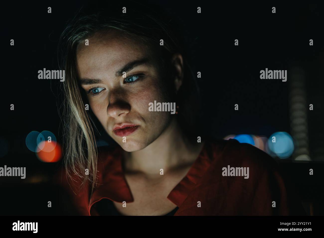 A woman is intensely focused on a screen, illuminated by its light in a ...