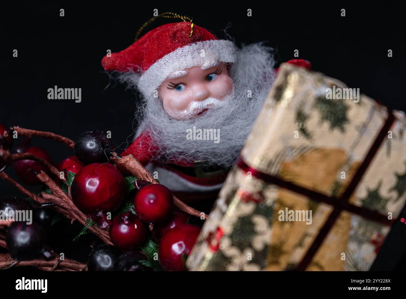 Little santa hiding behind mistletoe and christmas present on a black ...