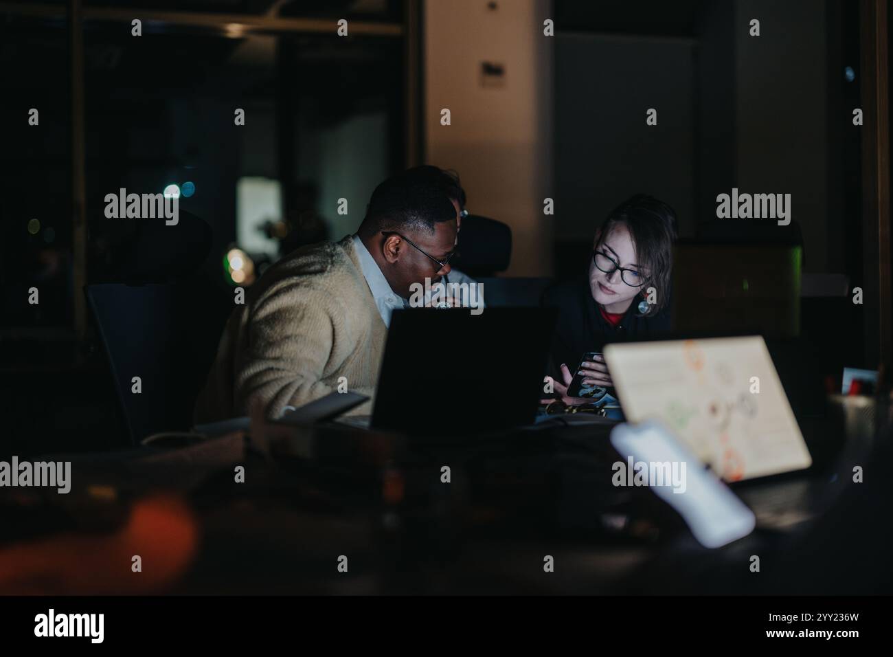Multiracial colleagues collaborating on project in dimly lit office environment Stock Photo - Alamy